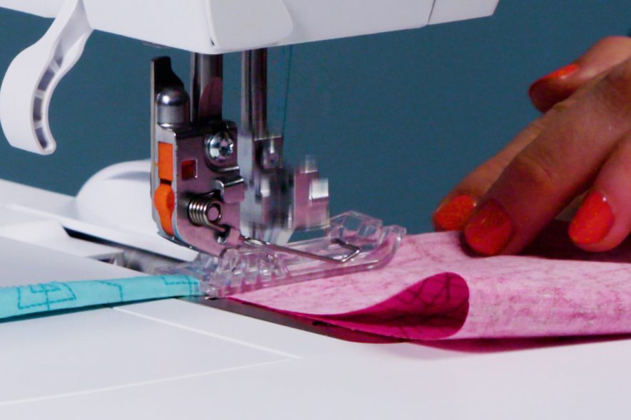 pink and blue fabric, with cording, being fed through a serger - WeAllSew